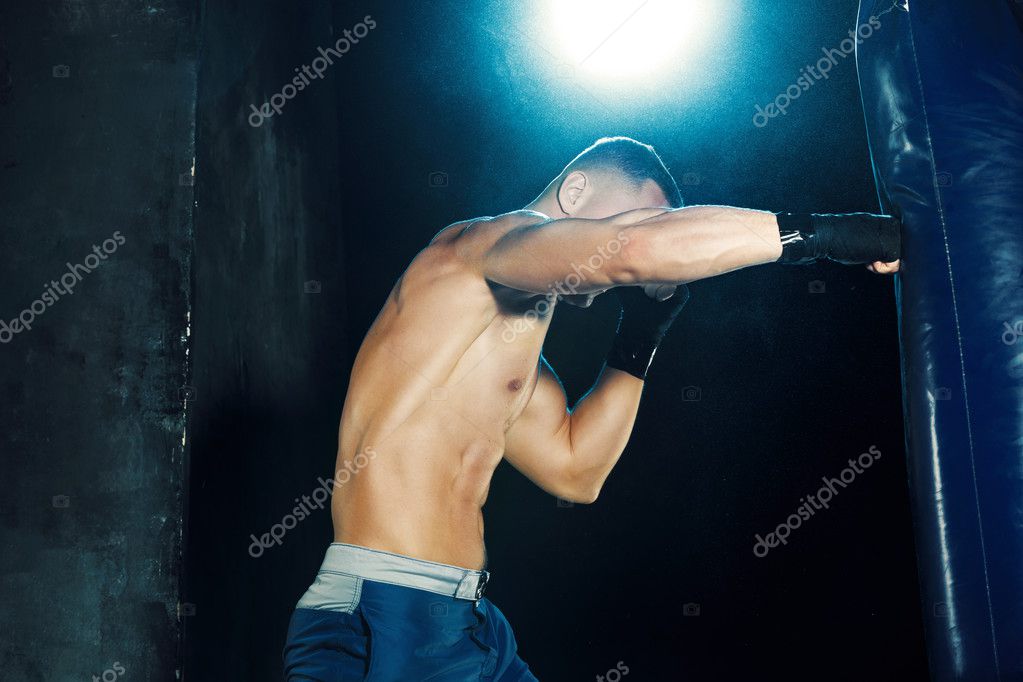 Male boxer boxing in punching bag with dramatic edgy lighting in a dark ...