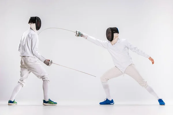 The two men wearing fencing suit practicing with sword against gray ...