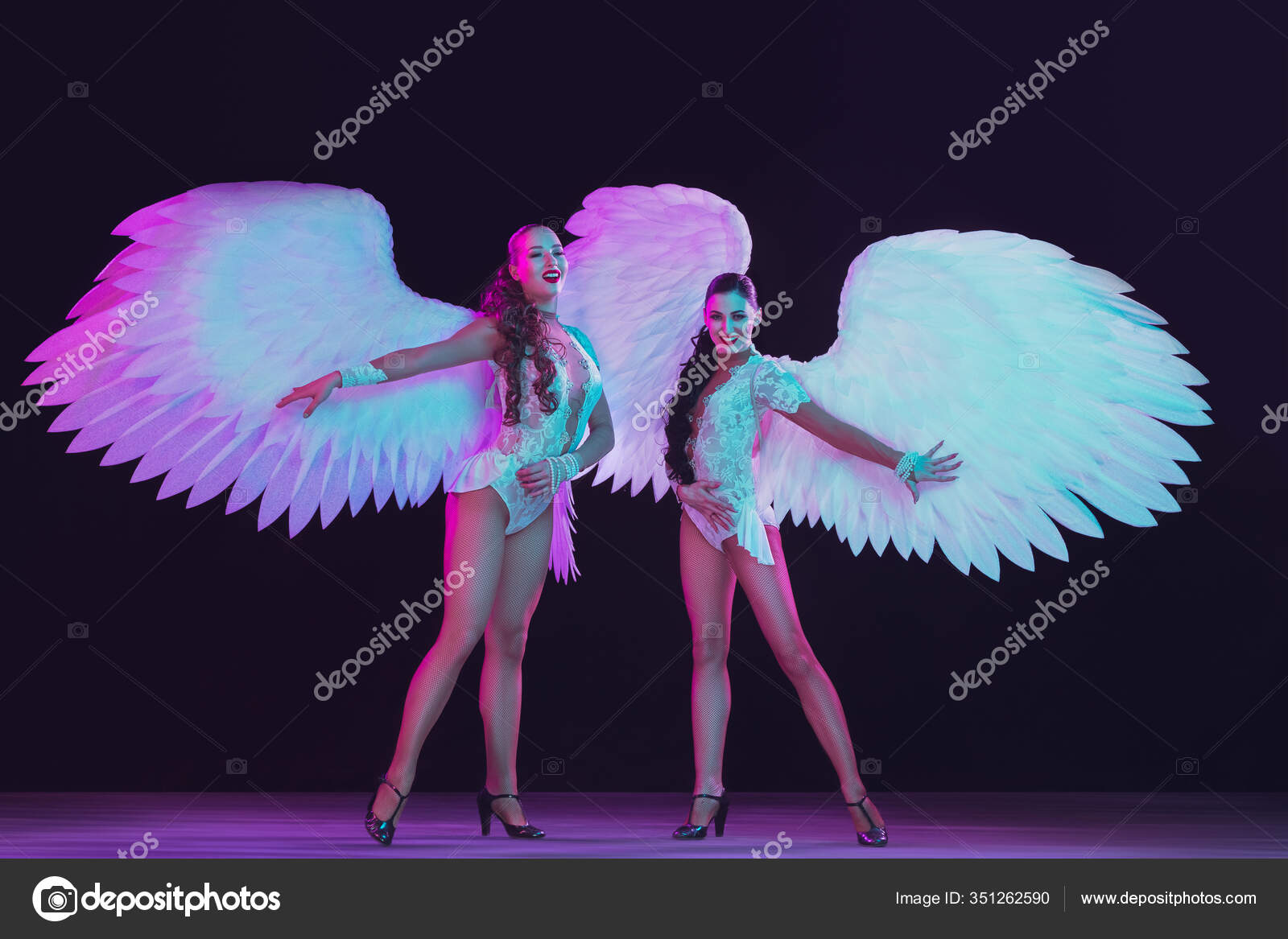 Young female dancers with angels wings in neon light on black ...