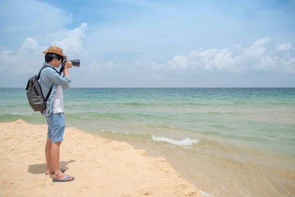 Profile of young man with camera in hand on beautiful white sandy beach ...