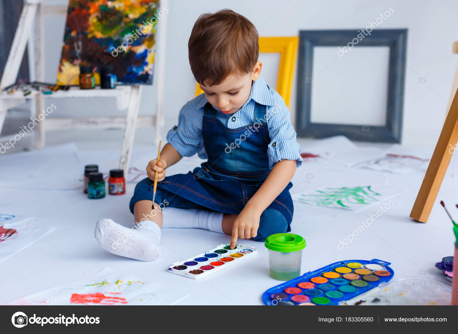 Cute, happy, white boy in blue shirt and jeans draws with paints ...