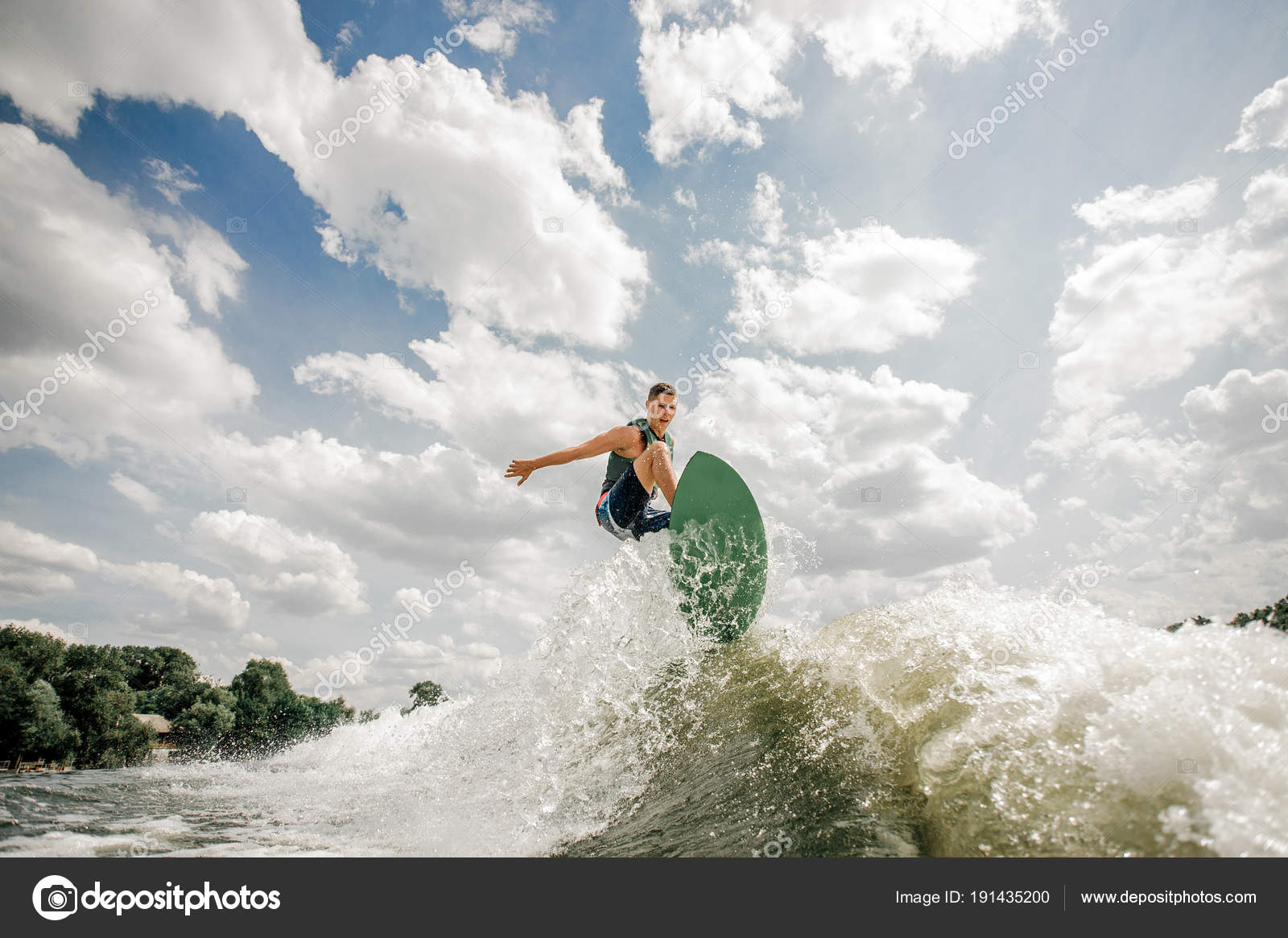 Young man having fun wakesurfing on the board down the river against ...