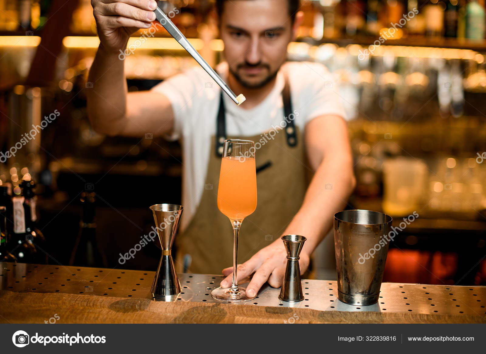 Professional male bartender adding with tweezers a little sugar cube to a cocktail in the glass ...