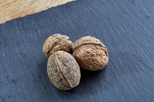 A stack of hard shells of walnuts piled together on dark piece of wood ...