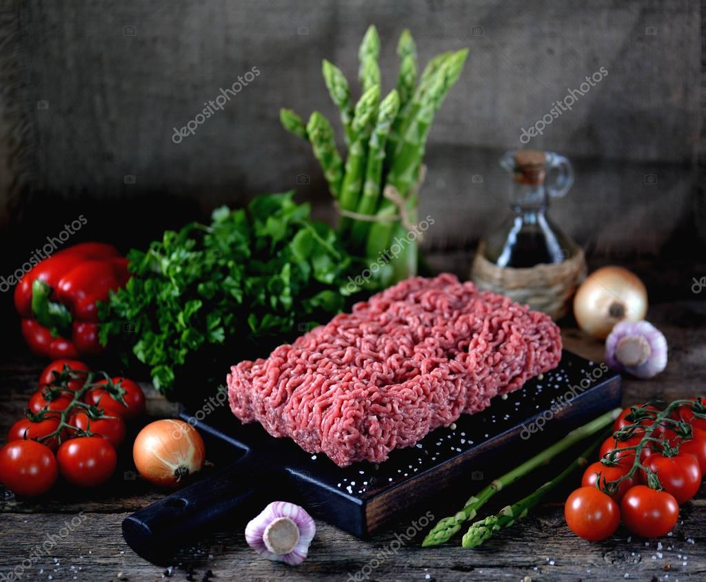 Carne fresca molida cruda con verduras frescas sobre un fondo de madera ...