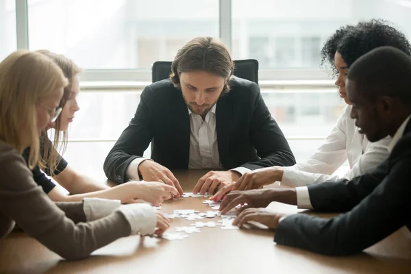 Diverse office team assembling puzzle helping finding business s ...