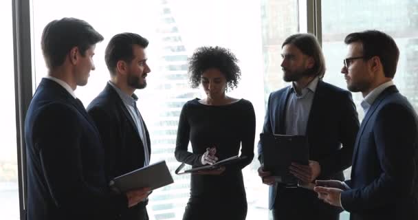Serious multi ethnic colleagues discuss project standing against office ... Serious multi ethnic colleagues discuss project standing against office ...