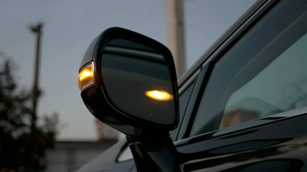 Car rear-view mirror. Direction indicator is flashing at evening ...