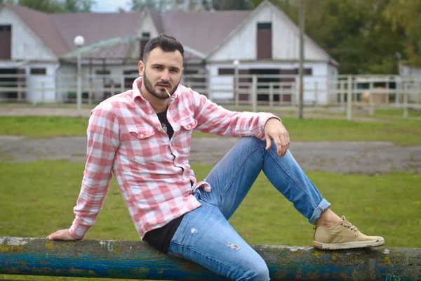 Young handsome guy Cowboy. male farmer is sitting on his fence on his ...