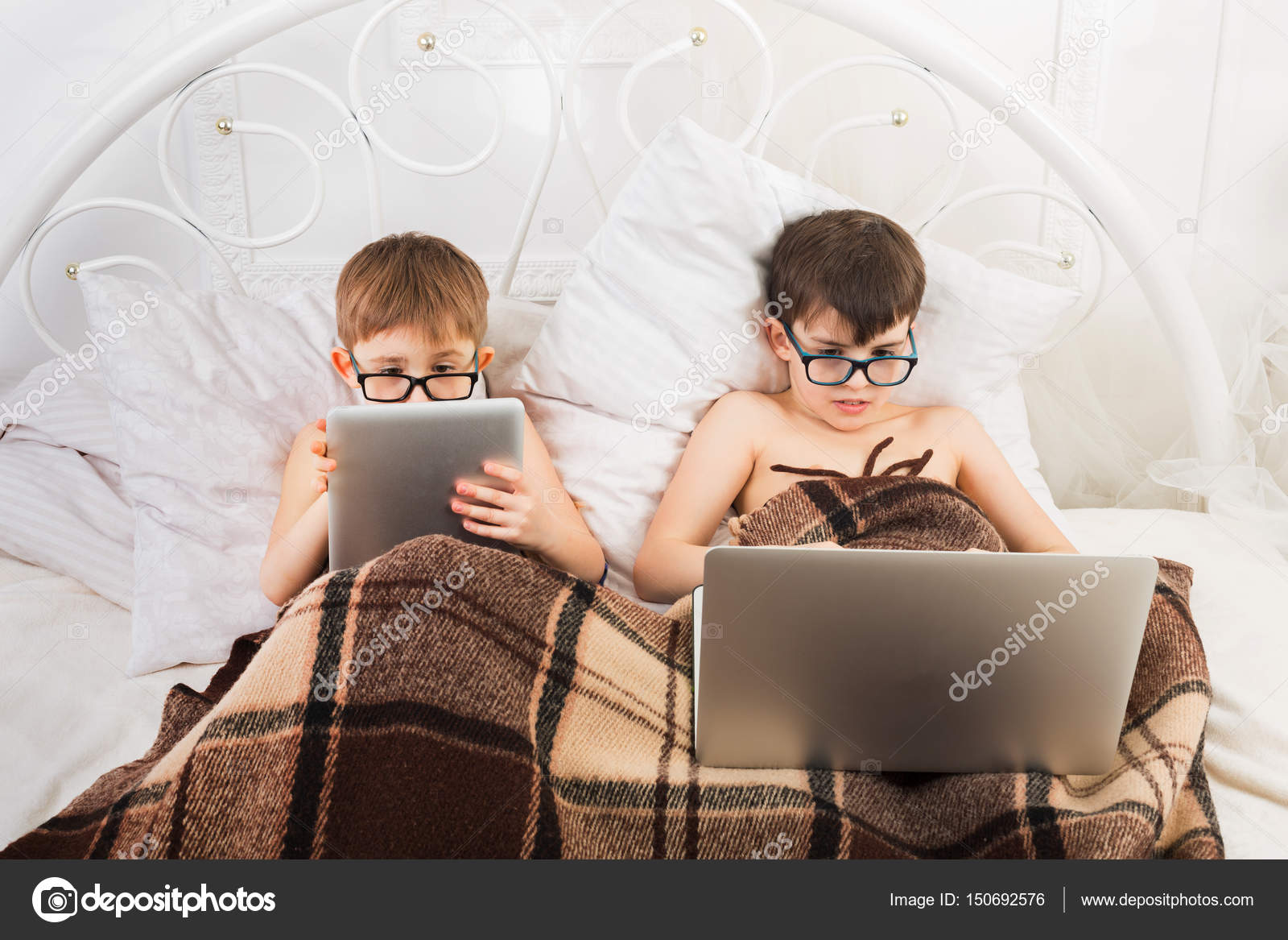 Two boys play at laptop and tablet with dog in bed Stock Photo by ...