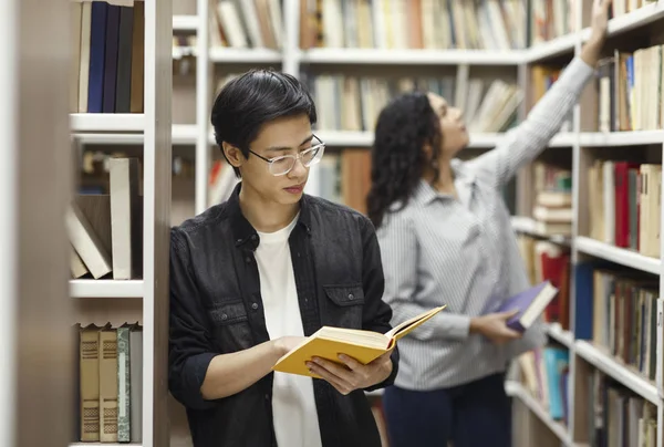 Focused japanese guy reading book at library - Stock Image - Everypixel