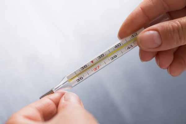 Mercury thermometer shows subfebrile temperature on a blue backg ...
