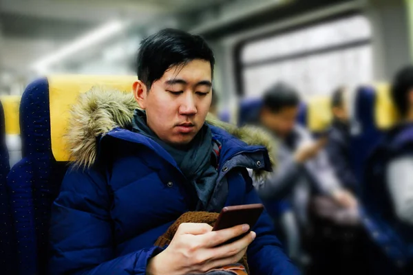 Asian man using smartphone on the public train in winter - Stock Image ...