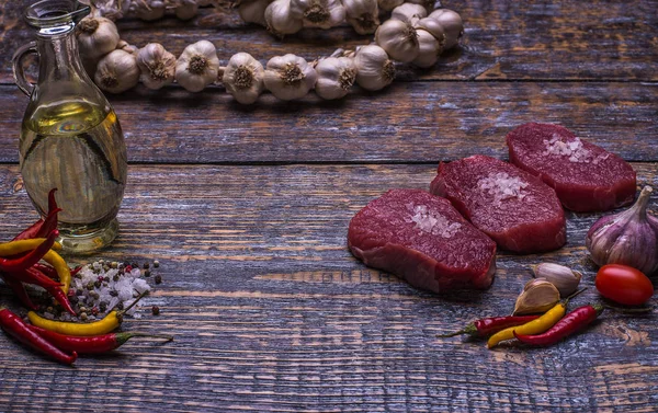 Raw Beef Steak, salt, pepper, garlic, rosemary on the black board ...