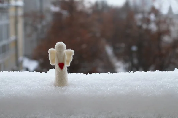 Woolen toy angel in the snow on the railing of the balcony against the ...
