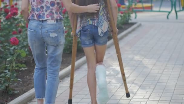 Mom Helps My Daughter With A Broken Leg On Crutches To Walk Along The