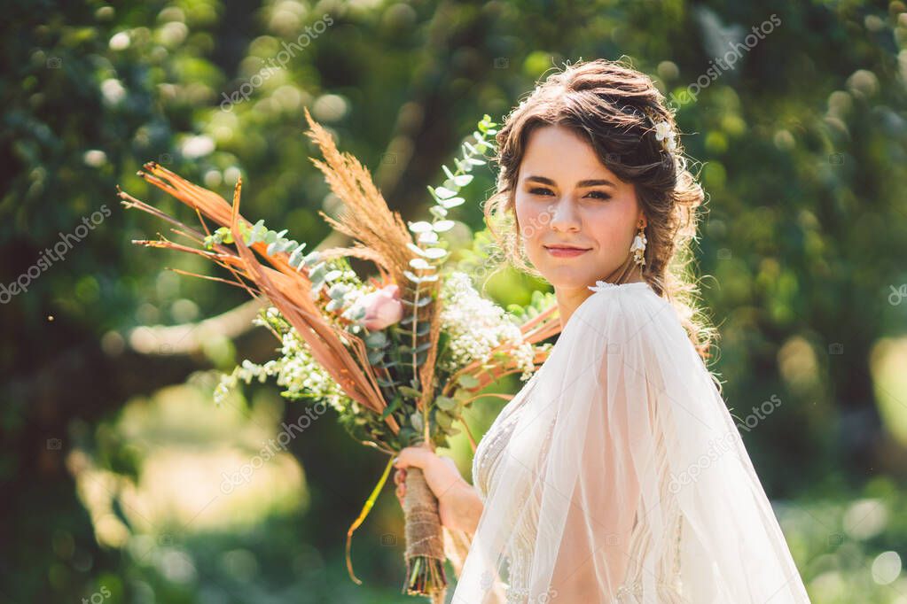 Hermosa novia con flores de ramo se encuentra en el fondo del bosque ...