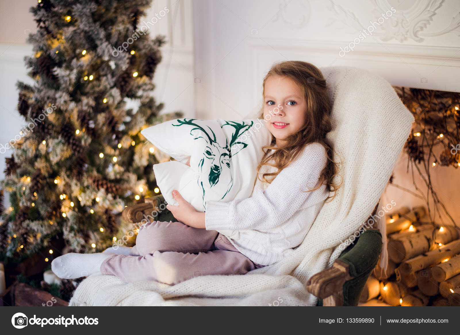 Little princess sit on armchair with deer pillow by Christmas tree at ...