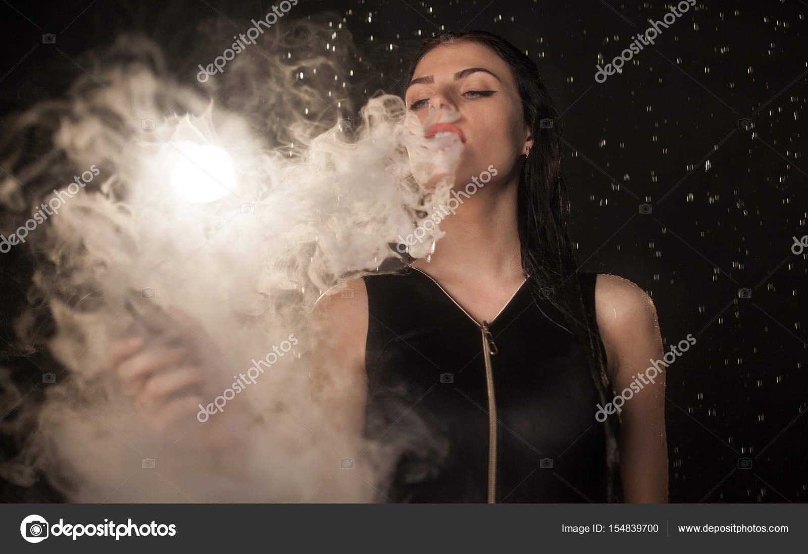 Young beautiful woman vaping e-cigarette. Water flowing on woman face ...