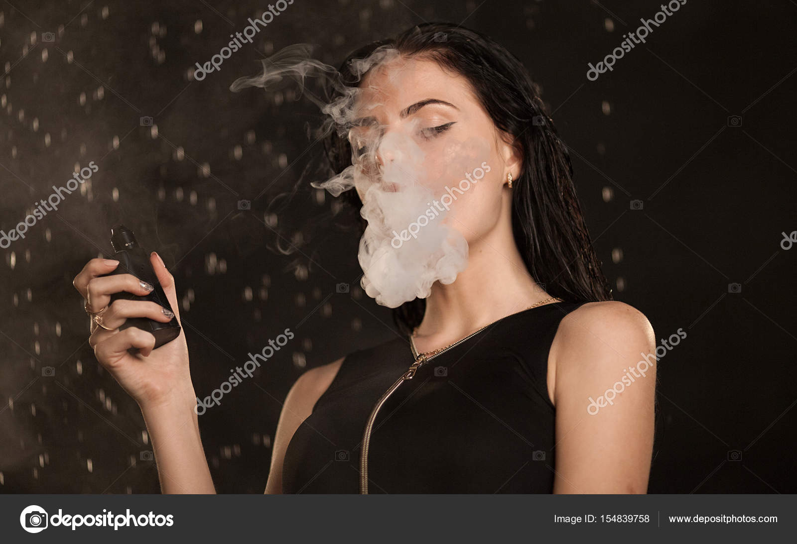 Young beautiful woman vaping e-cigarette. Water flowing on woman face ...