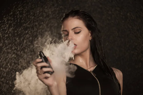 Young beautiful woman vaping e-cigarette. Water flowing on woman face ...