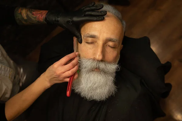 Shaving process of beards in Barbershop. Master makes a haircut beard ...