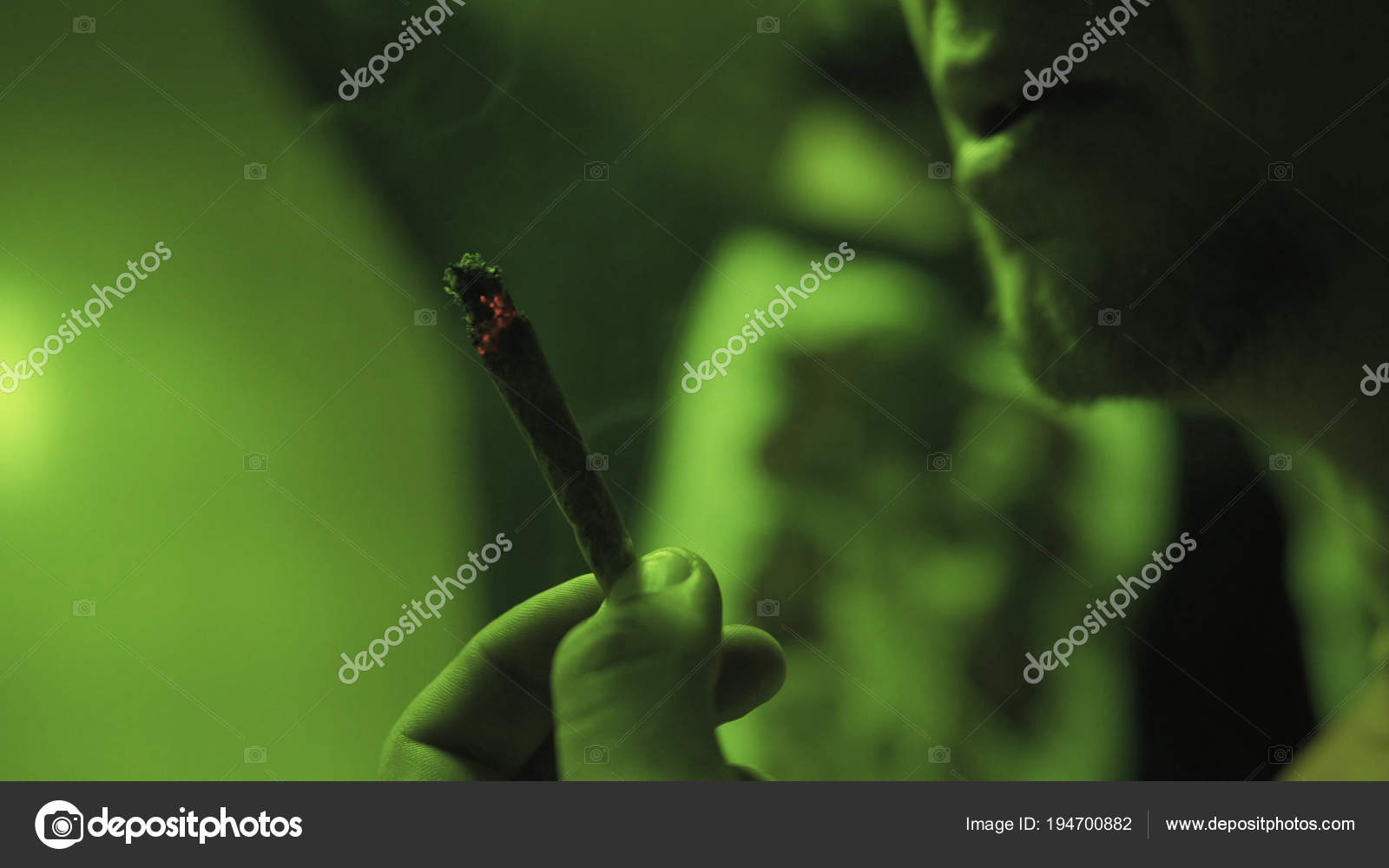 A young guy smoking a rolled jointer with weed buds inside in the green ...