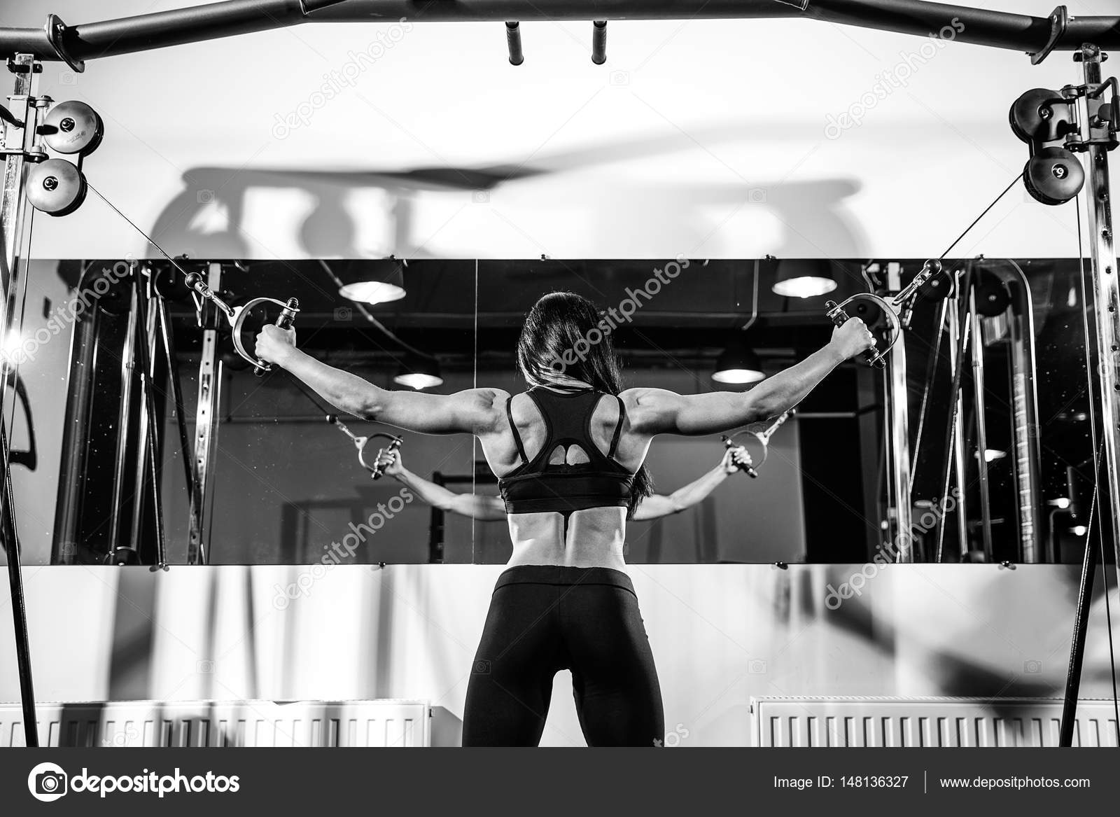 Woman flexing muscles on cable machine in gym. exercise on biceps. back ...