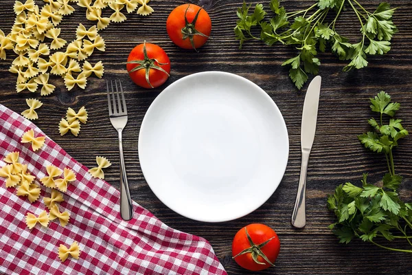 Table setting with cutlery, pasta, tomatoes and herb on dark woo ...