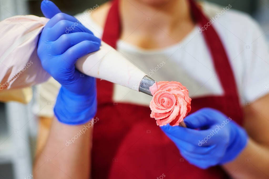 El chef de pasteler a hace una flor de rosa con crema de mantequilla para decorar el pastel. La ...