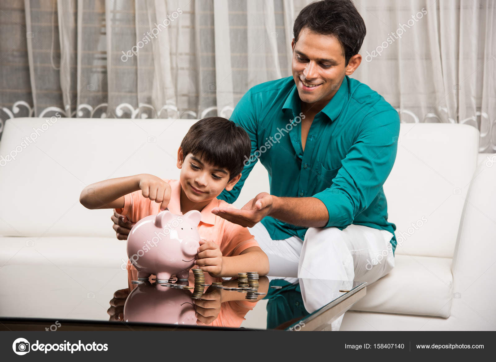 Indian Father and Son putting coins into pink piggy bank, teaching ...