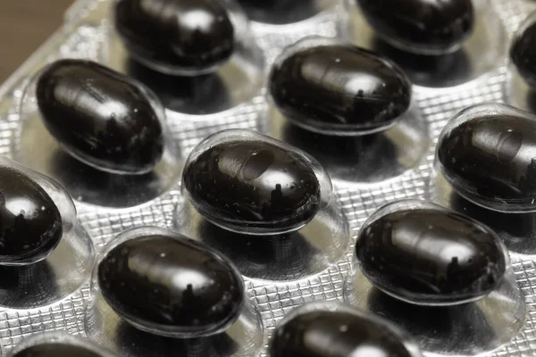 Black pills are seen in a blister black up-close, oval shaped capsules ...