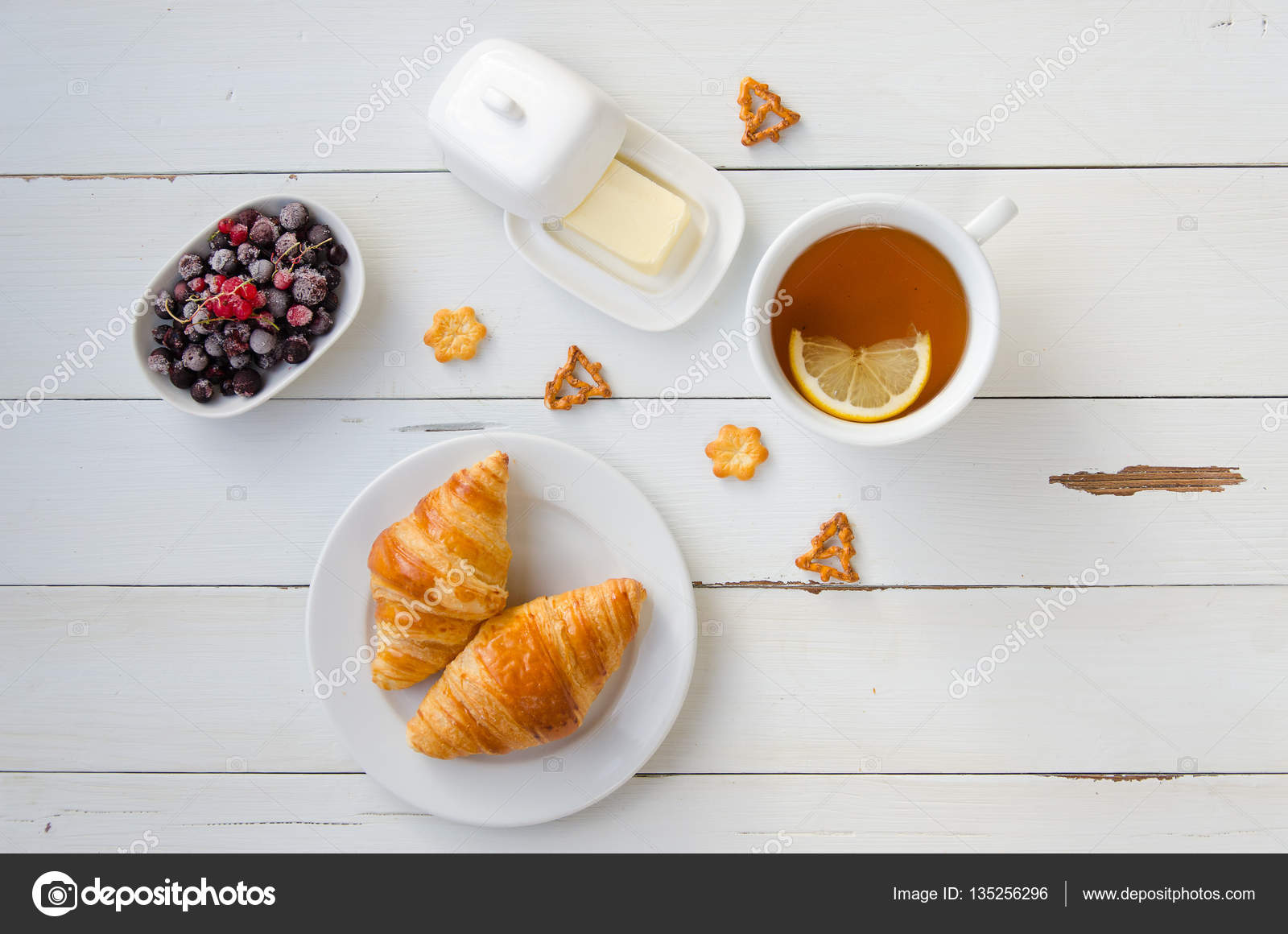 Breakfast from hot croissants, butter,tea and currants on wooden table ...