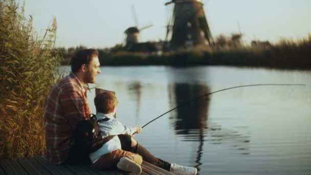 European father and son sit together on lake pier. Boy holds a hand ...