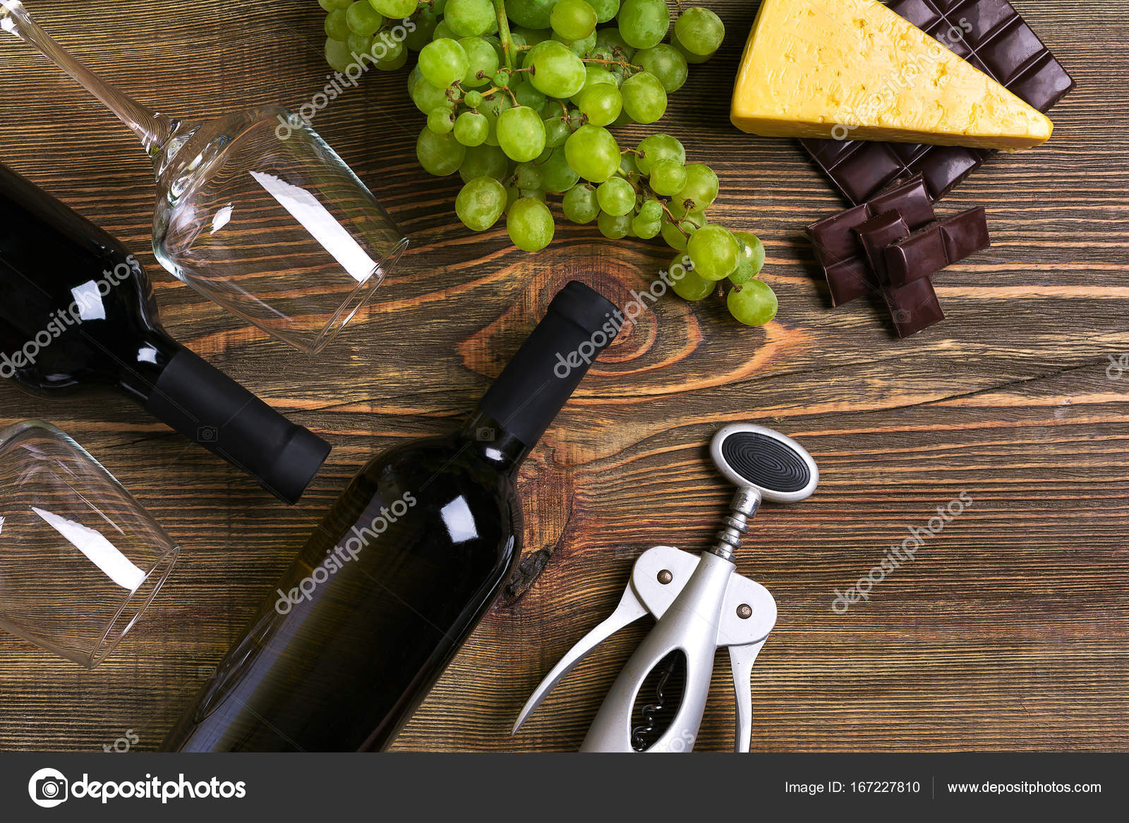 Red and white wine bottles, grape, cheese and glasses over wooden table ...