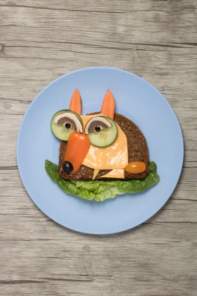 Fox made with bread, cheese and vegetables on plate and wooden ...