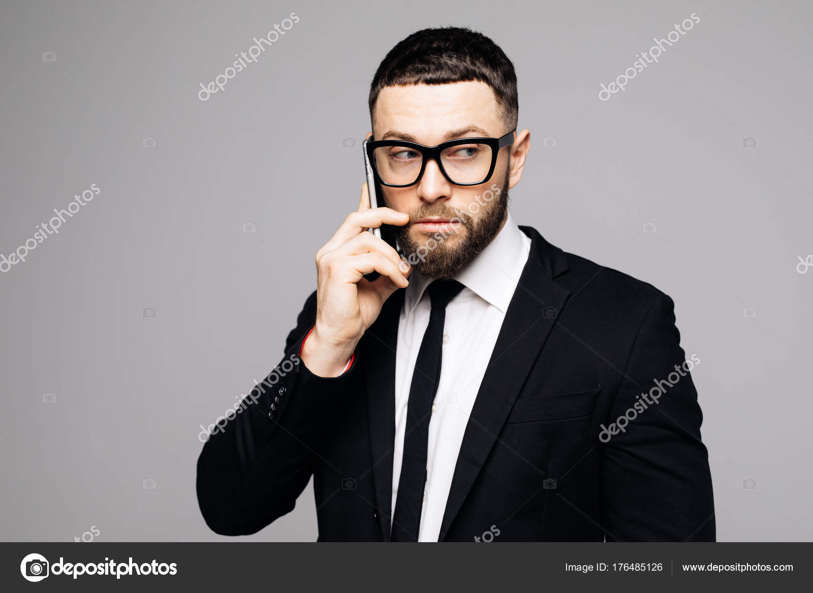 Portrait of serious young attractive man in black suit talking on ...