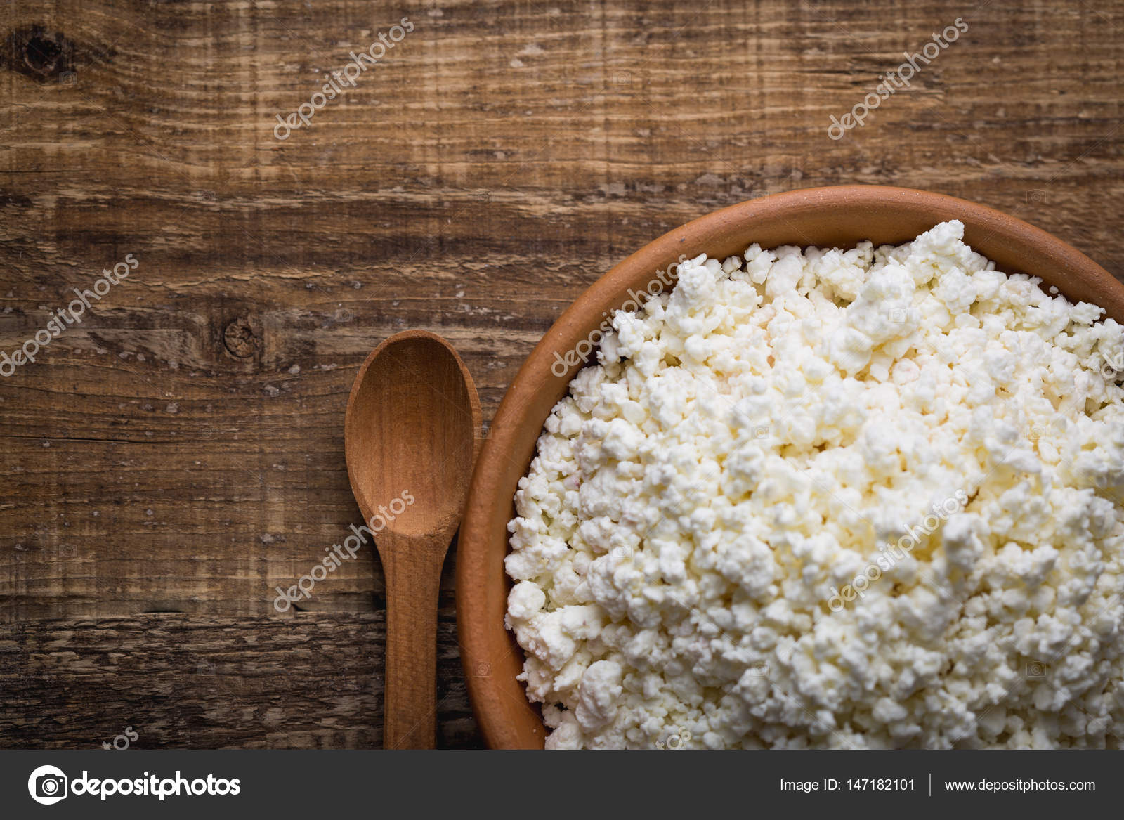 Cottage cheese in a clay pot with a wooden spoon closeup on wooden ...