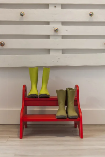 Green rain boots on red two steps ladder. White pallet backgroun ...