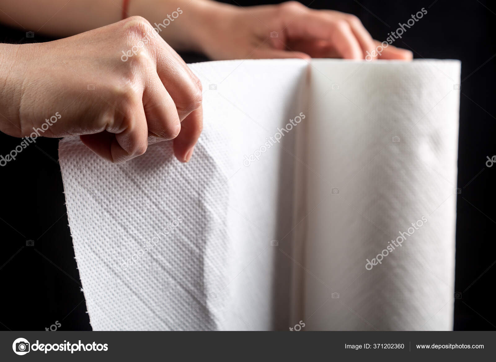 Hands tear off a piece of white paper towel from a roll on a black ...