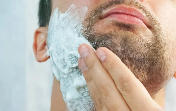 Close up of man face applying a foam on his chin on a light back ...