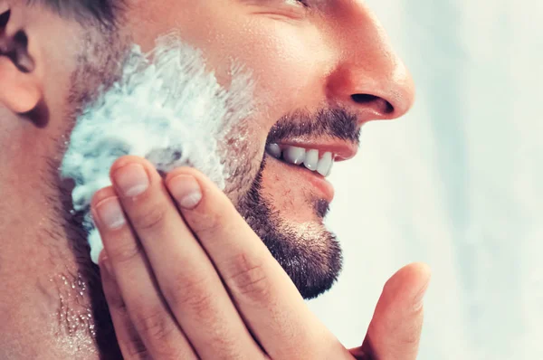 A young man is shaving in the morning, smiling. On the face ther - Stock Image - Everypixel