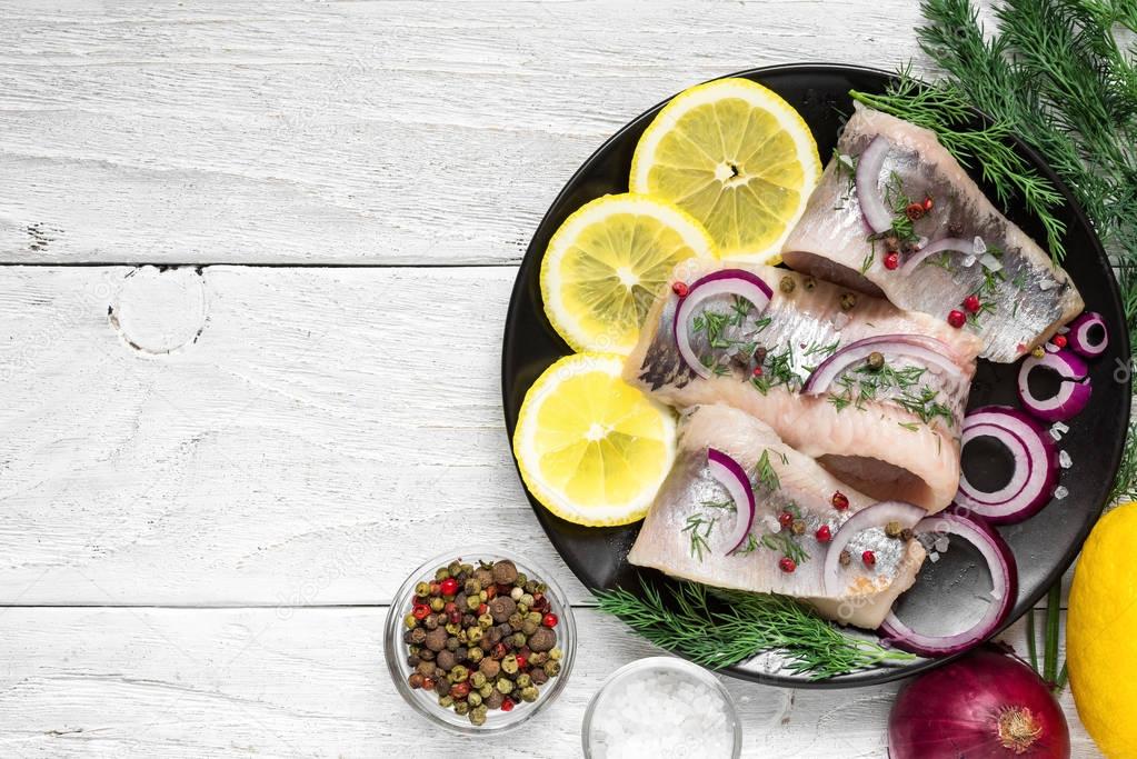 Filete de arenque con sal, pimienta, hierbas, cebolla y limón en plato ...