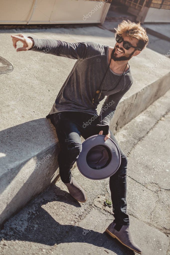 Emocionado hombre riendo y señalando mientras está sentado en la pared 2022