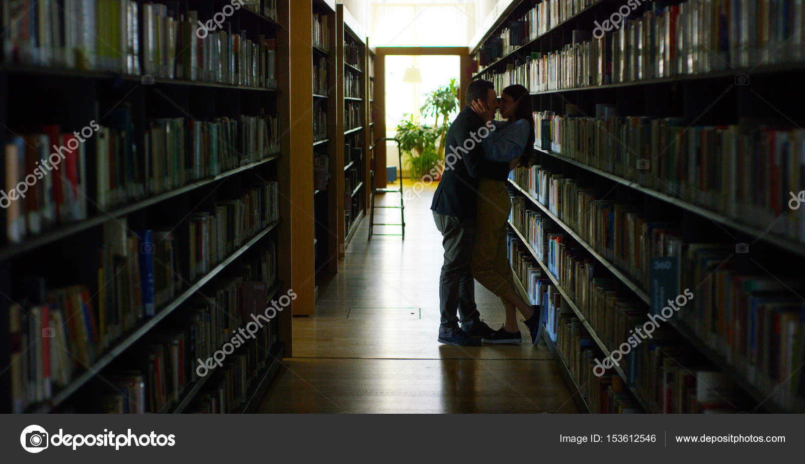 In a library, a couple in love, kissing and hug and carried away by ...