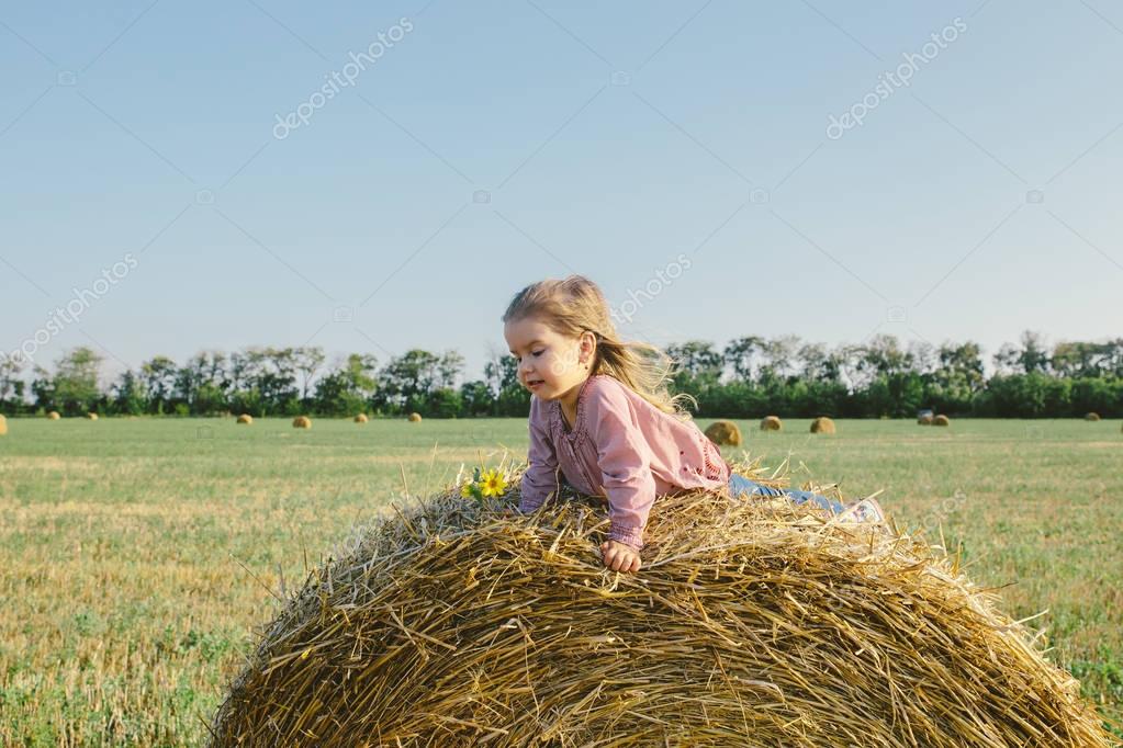 Little girl sitting on a haystack — Stock Photo © skvalval #129198994