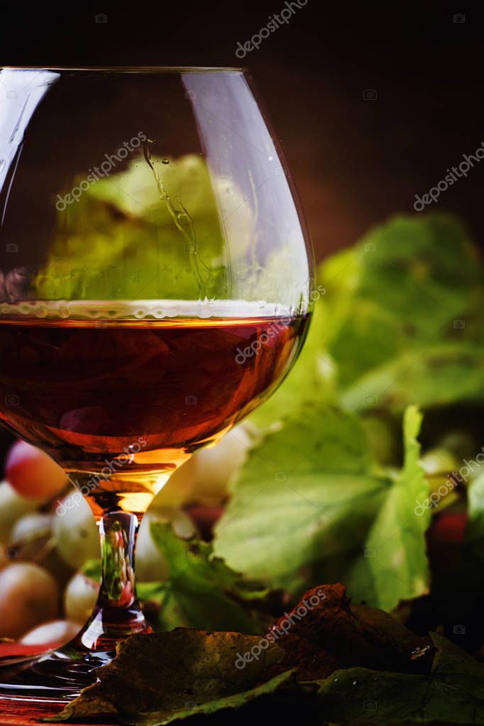 Brandy en un vaso y uvas frescas con hojas y una vid, naturaleza muerta ...