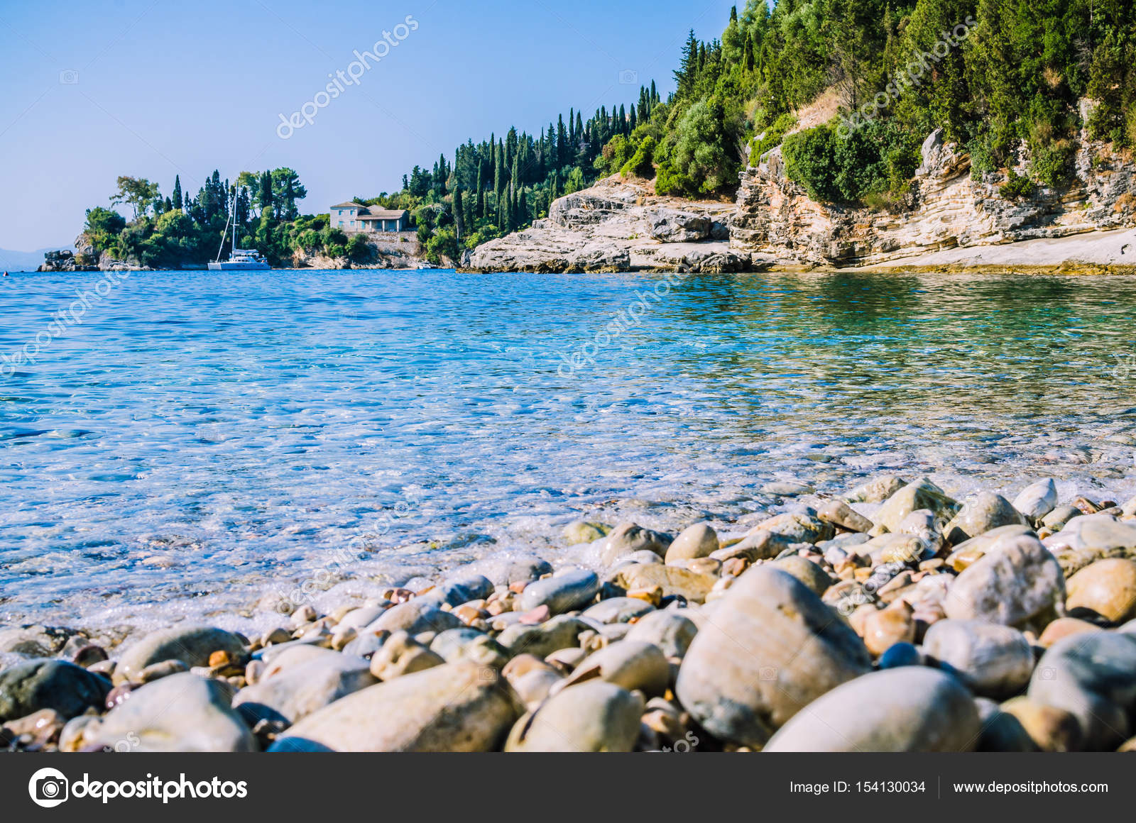 Pebble beach near Kalami with pine and cypress trees and an yacht at ...