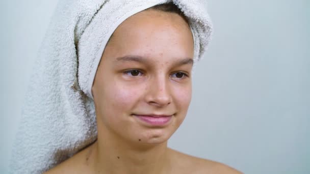 Amiable teenager wrapped in bath towels smiling at camera in white ...