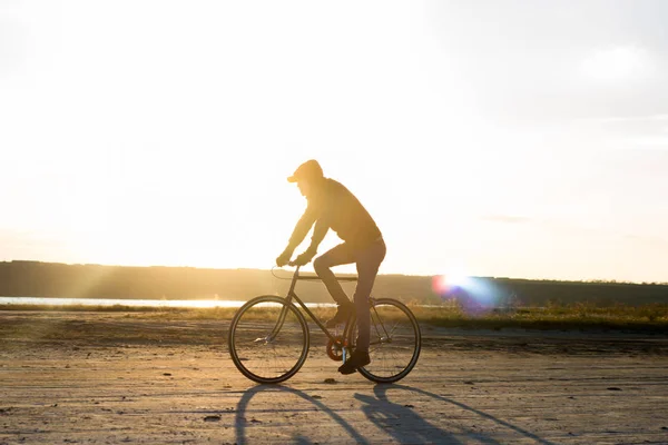 Alone rider on fixed gear road bike riding in the desert near river ...